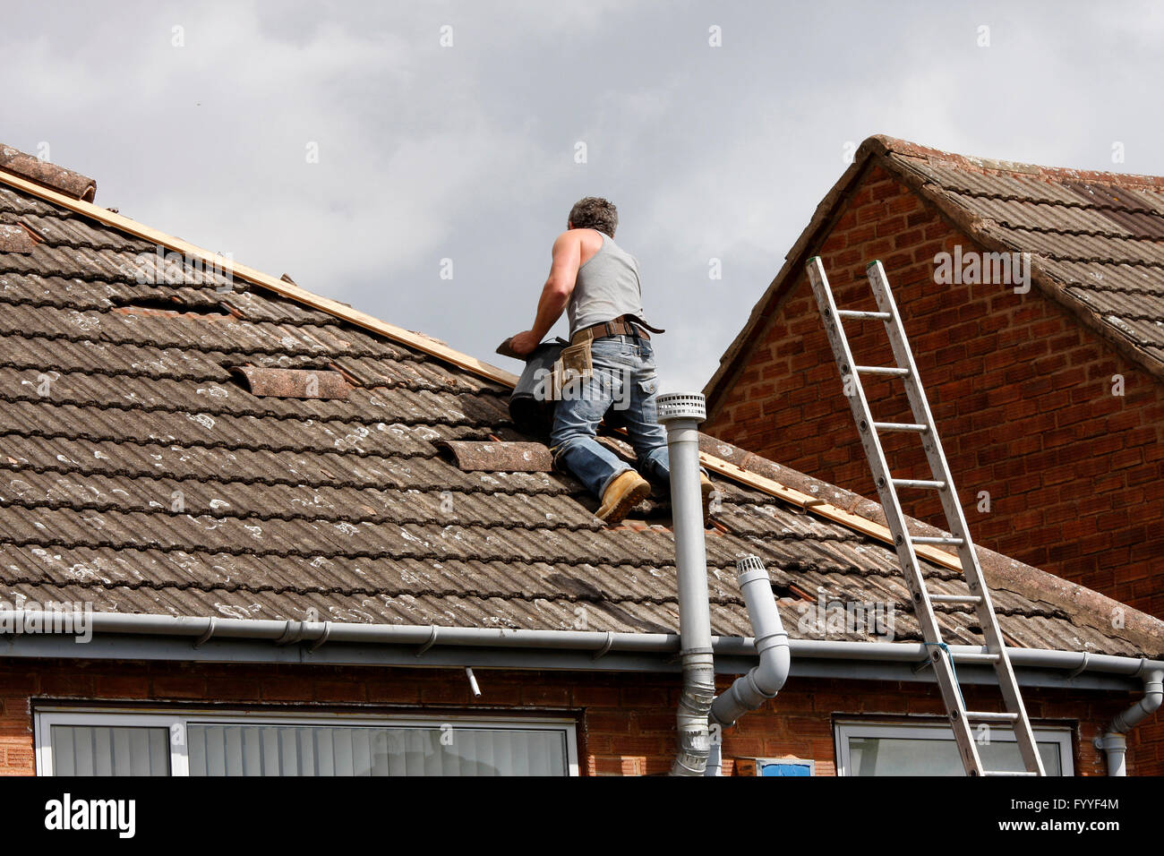 Workman repairing the ridge tiles on a roof Stock Photo - Alamy