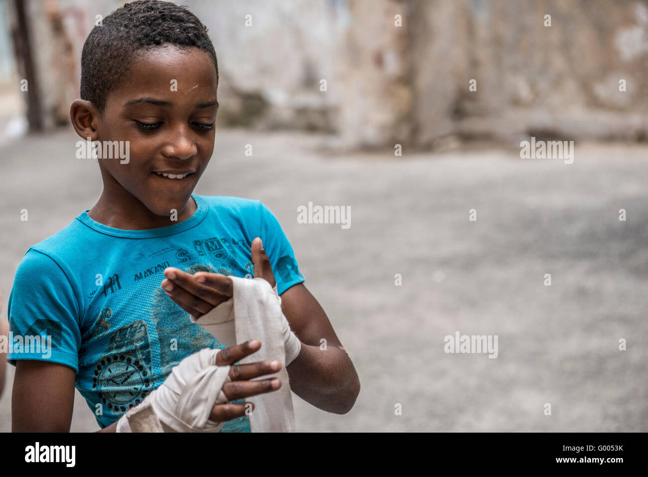 A young Cuban boy looks happy with his boxing wraps as he prepares for ...