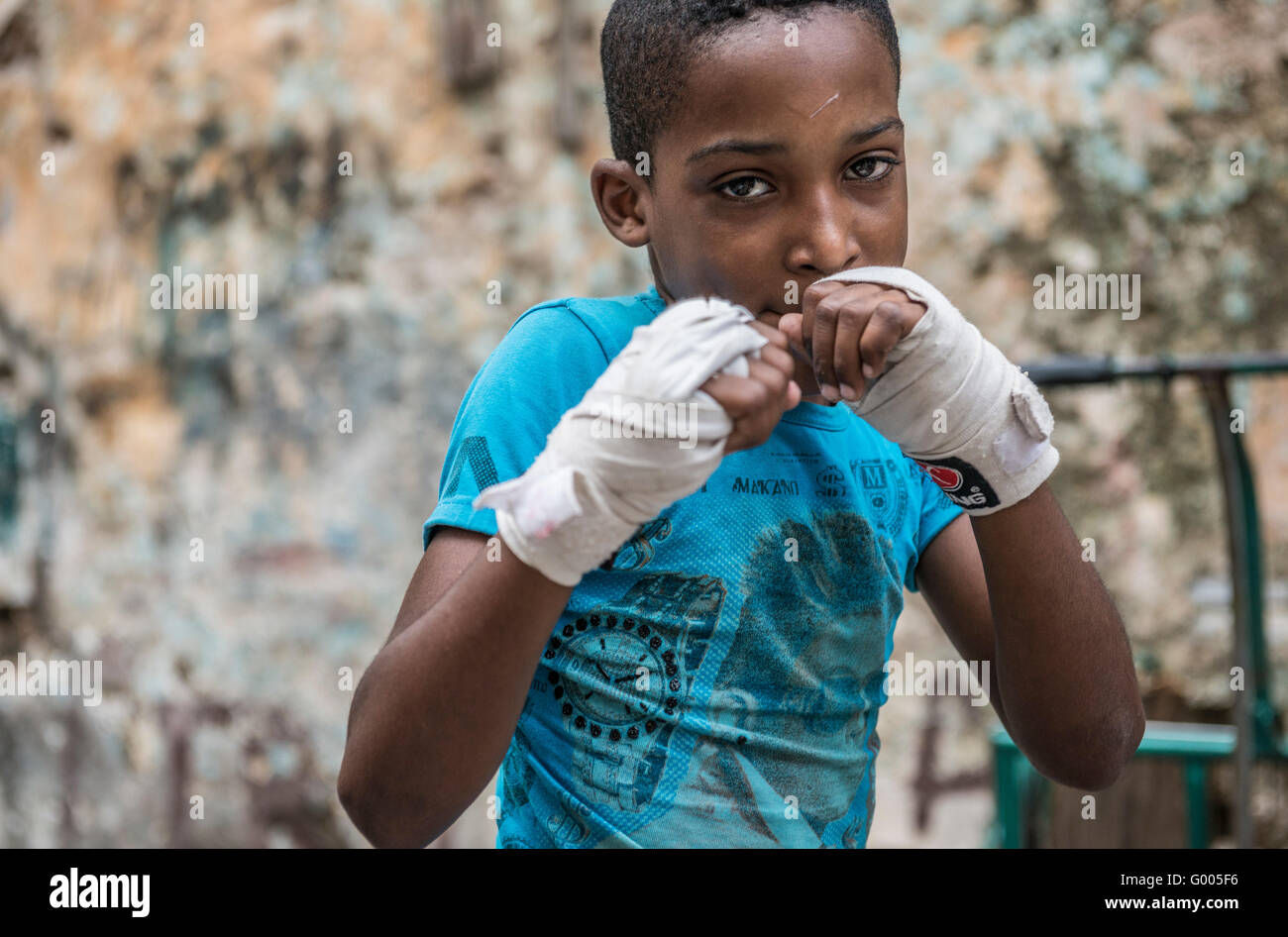 A serious young Cuban boy takes a sparring stance, wearing boxing wraps ...