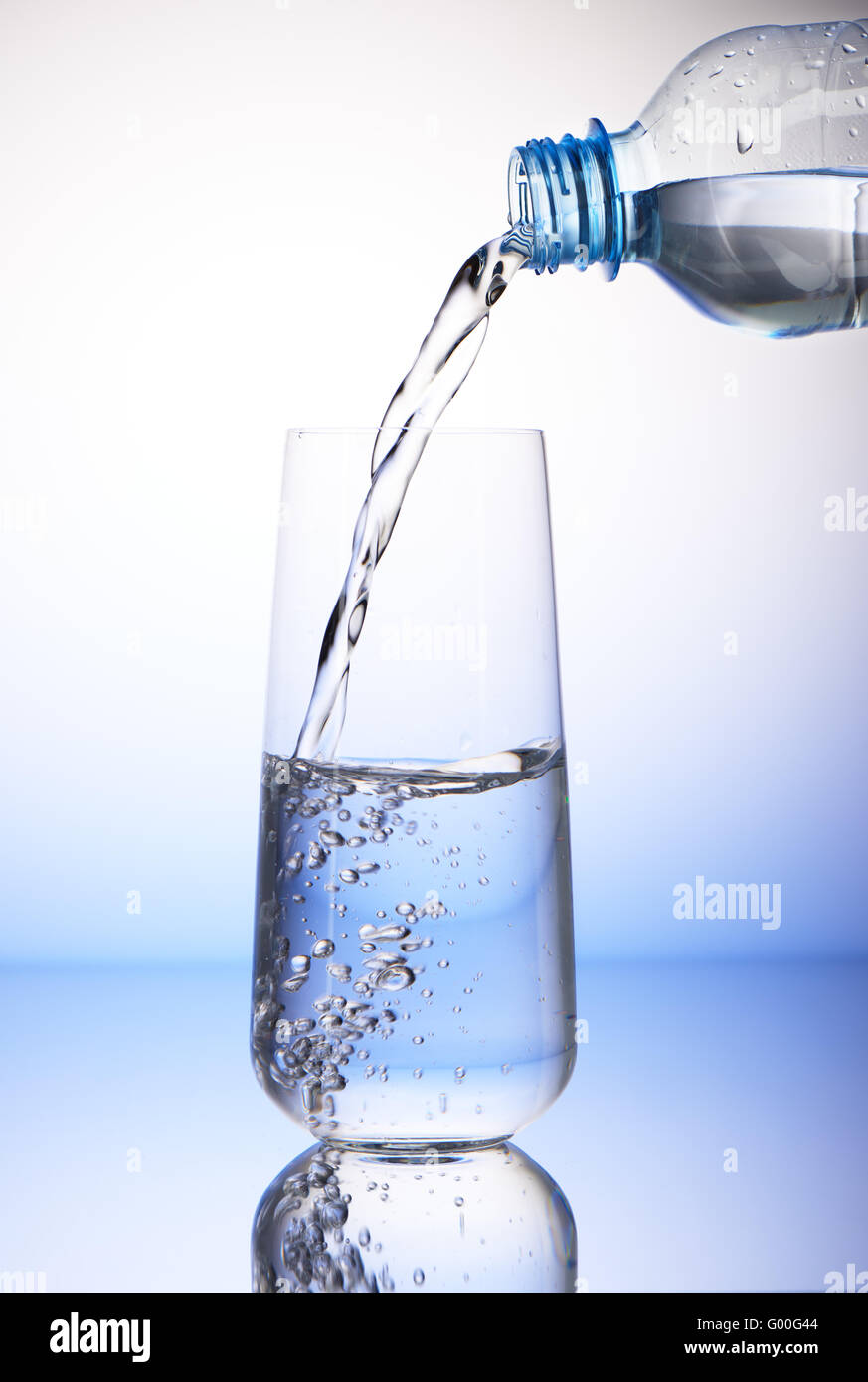 Water pouring from plastic bottle into half-filled drinking glass with ...