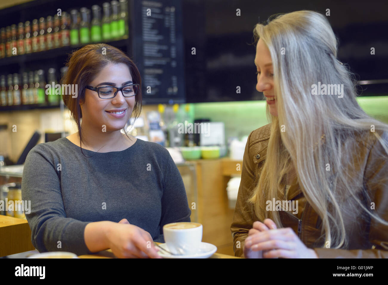Young waitress serving a cup of coffee to a pretty young female ...