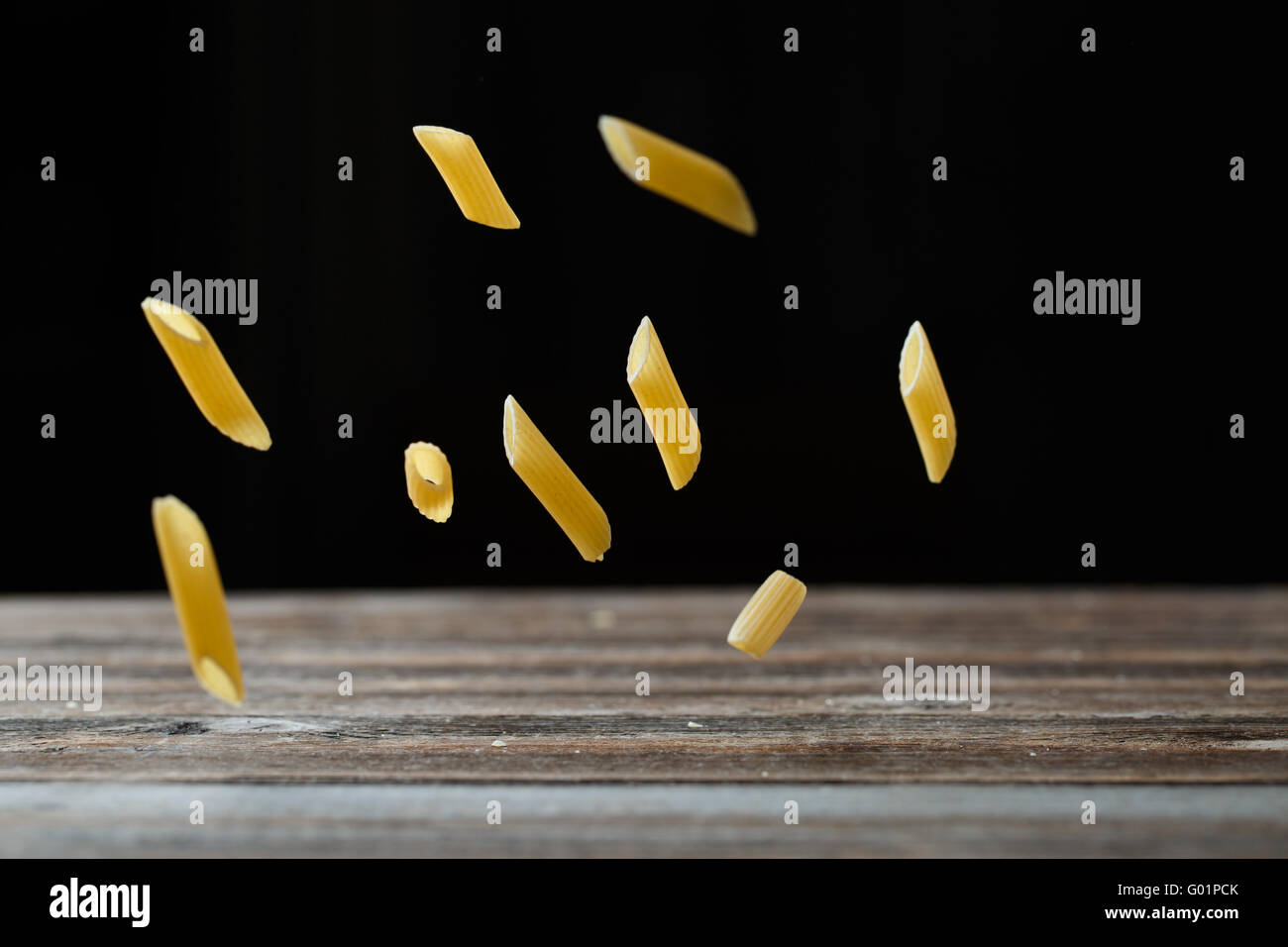 Falling penne pasta. Flying yellow raw macaroni over black background ...