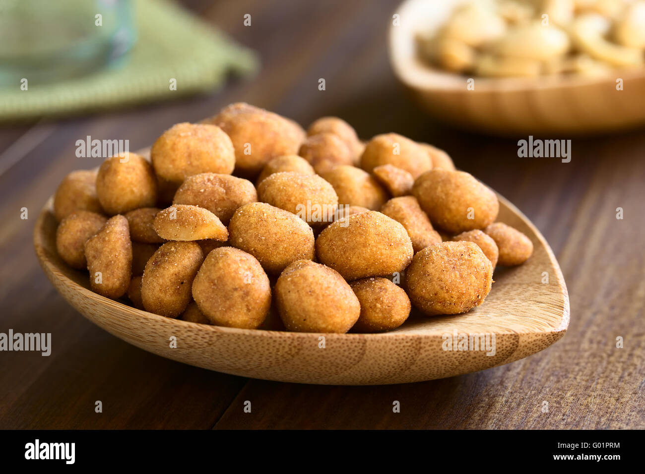 Roasted peanuts in spicy coat, photographed on dark wood with natural ...