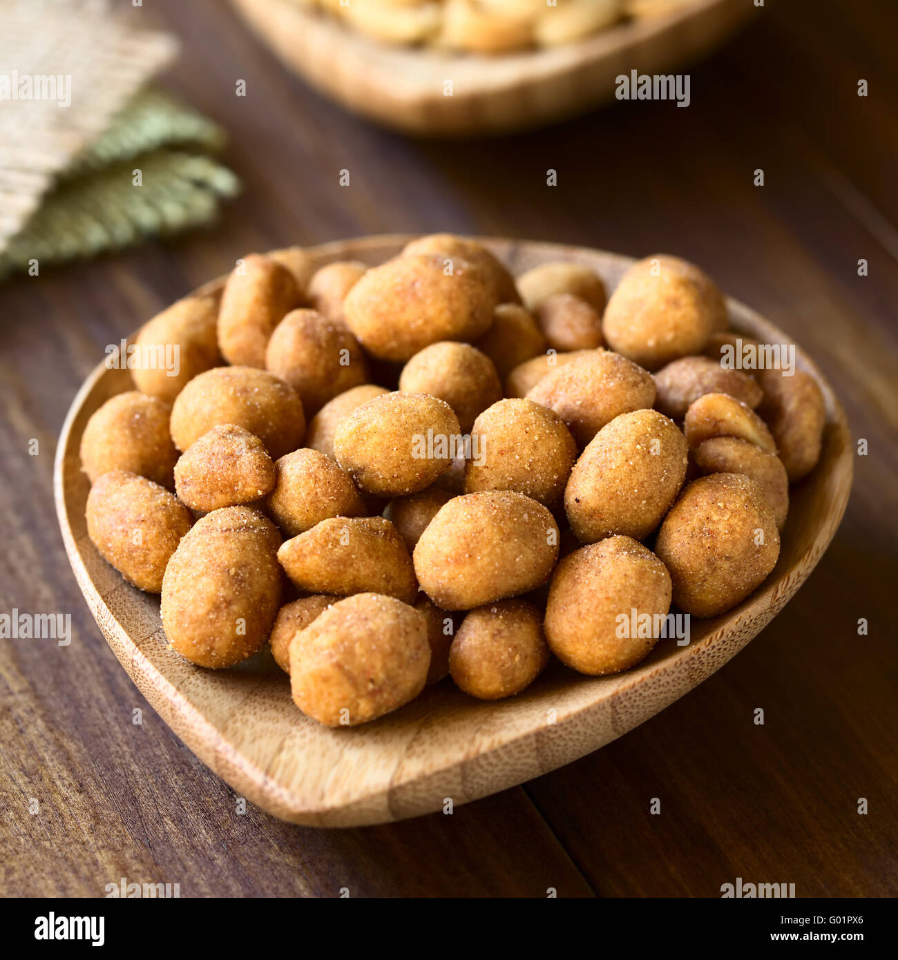 Roasted peanuts in spicy coat, photographed on dark wood with natural ...
