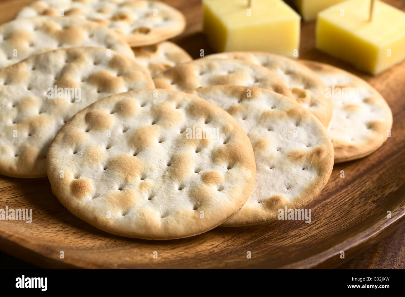 Saltine or soda crackers with cheese pieces on wooden plate ...