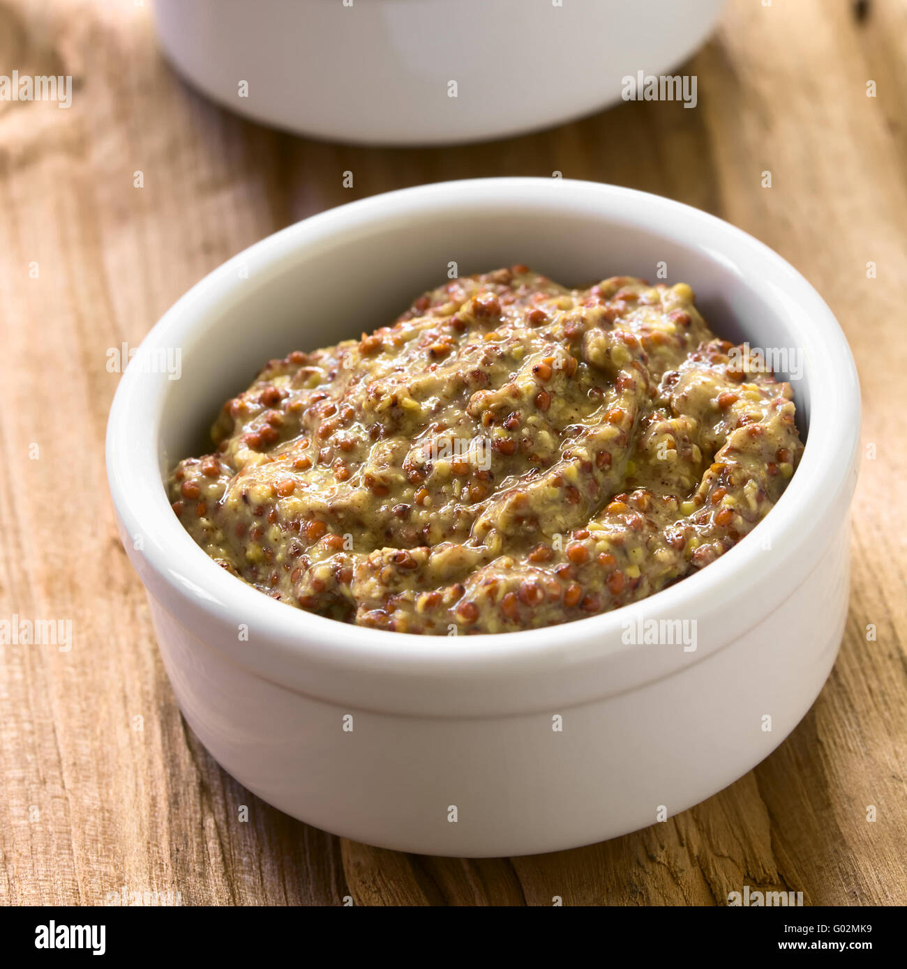 Whole grain mustard in small bowl, photographed on wood with natural ...