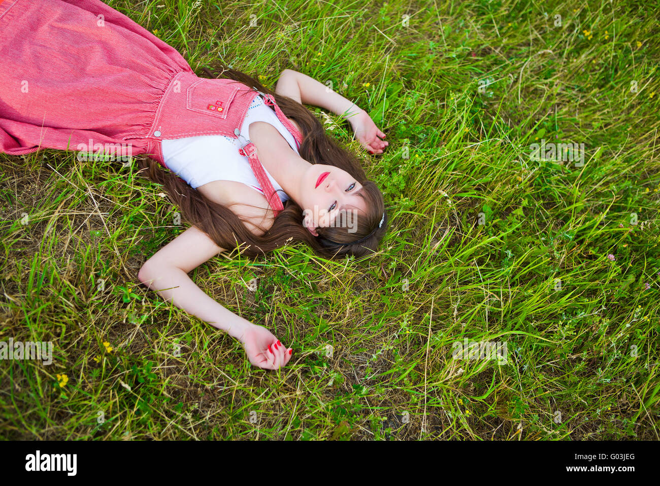Pretty girl in red sarafan lies on the green grass Stock Photo - Alamy