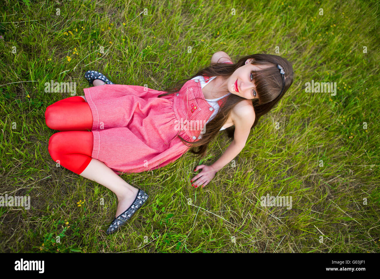 Pretty girl in red sarafan lies on the green grass Stock Photo - Alamy