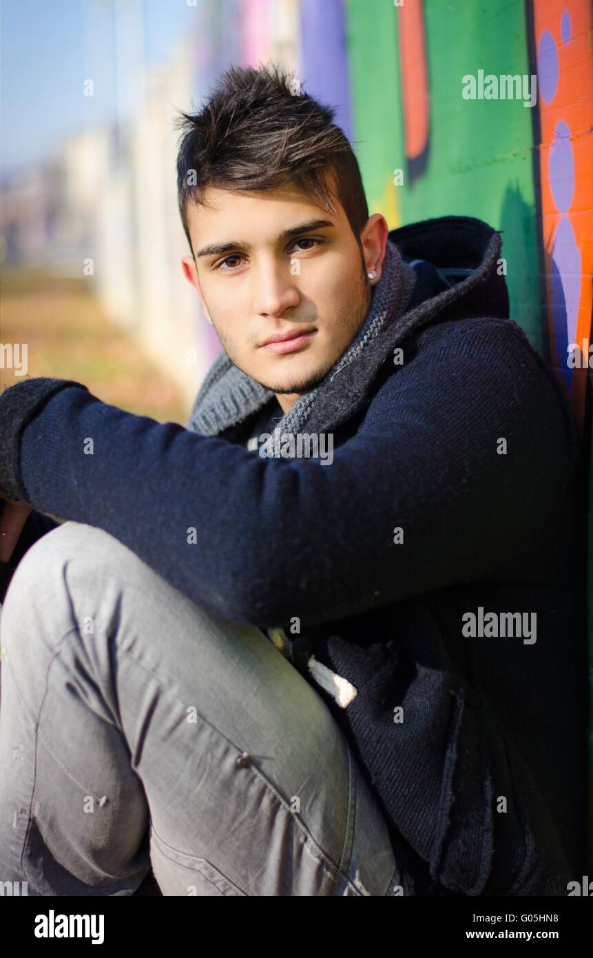 Handsome young man sitting against colorful graffiti Stock Photo - Alamy