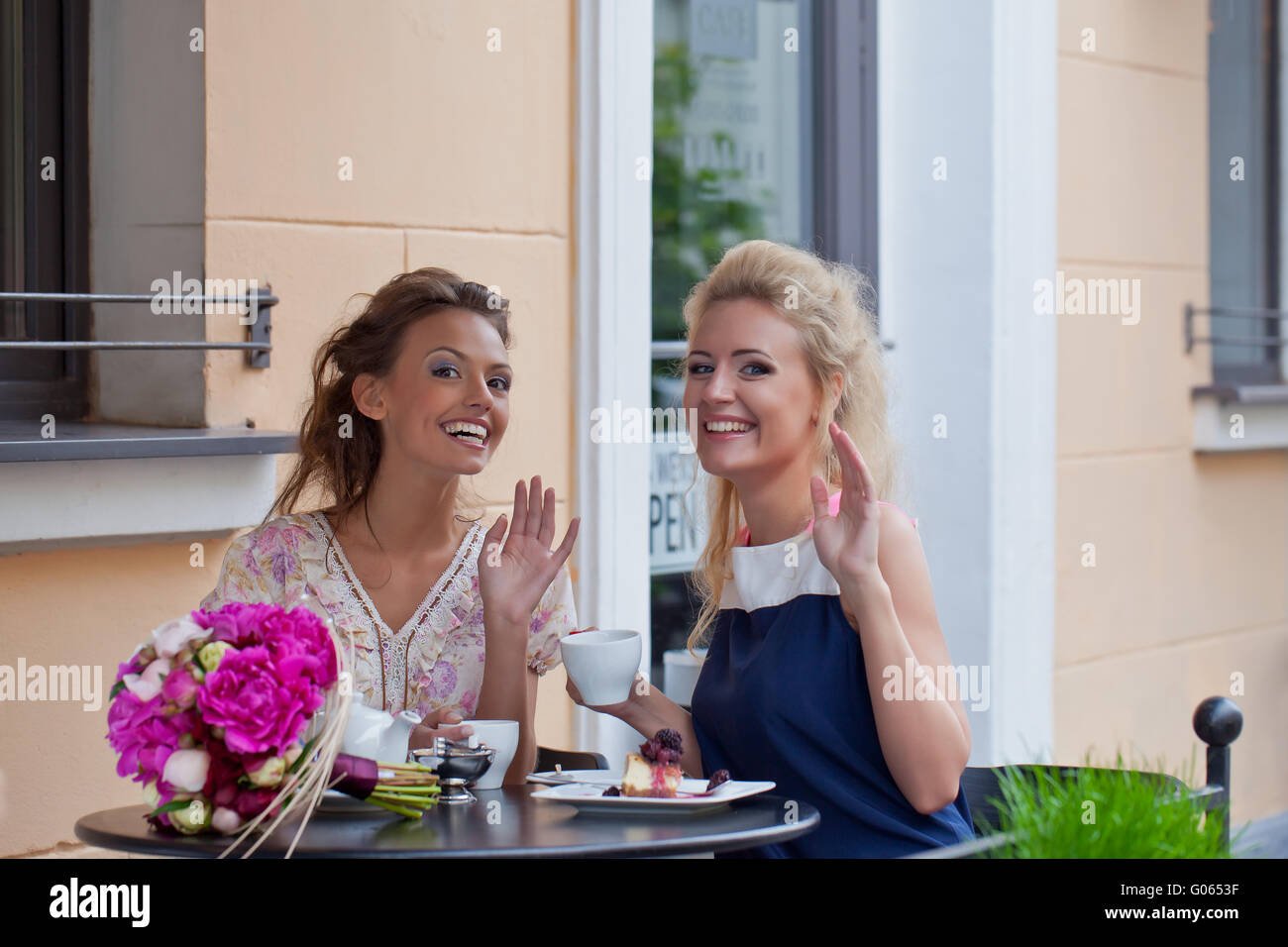 two beautiful young girls in summer outfit have lunch at the table in ...