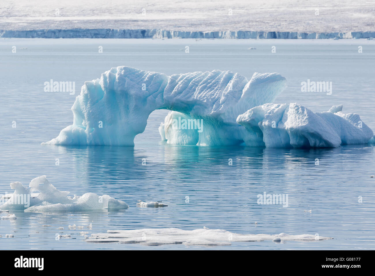 An iceberg with a natural arch reflecting in the water as it drifts ...