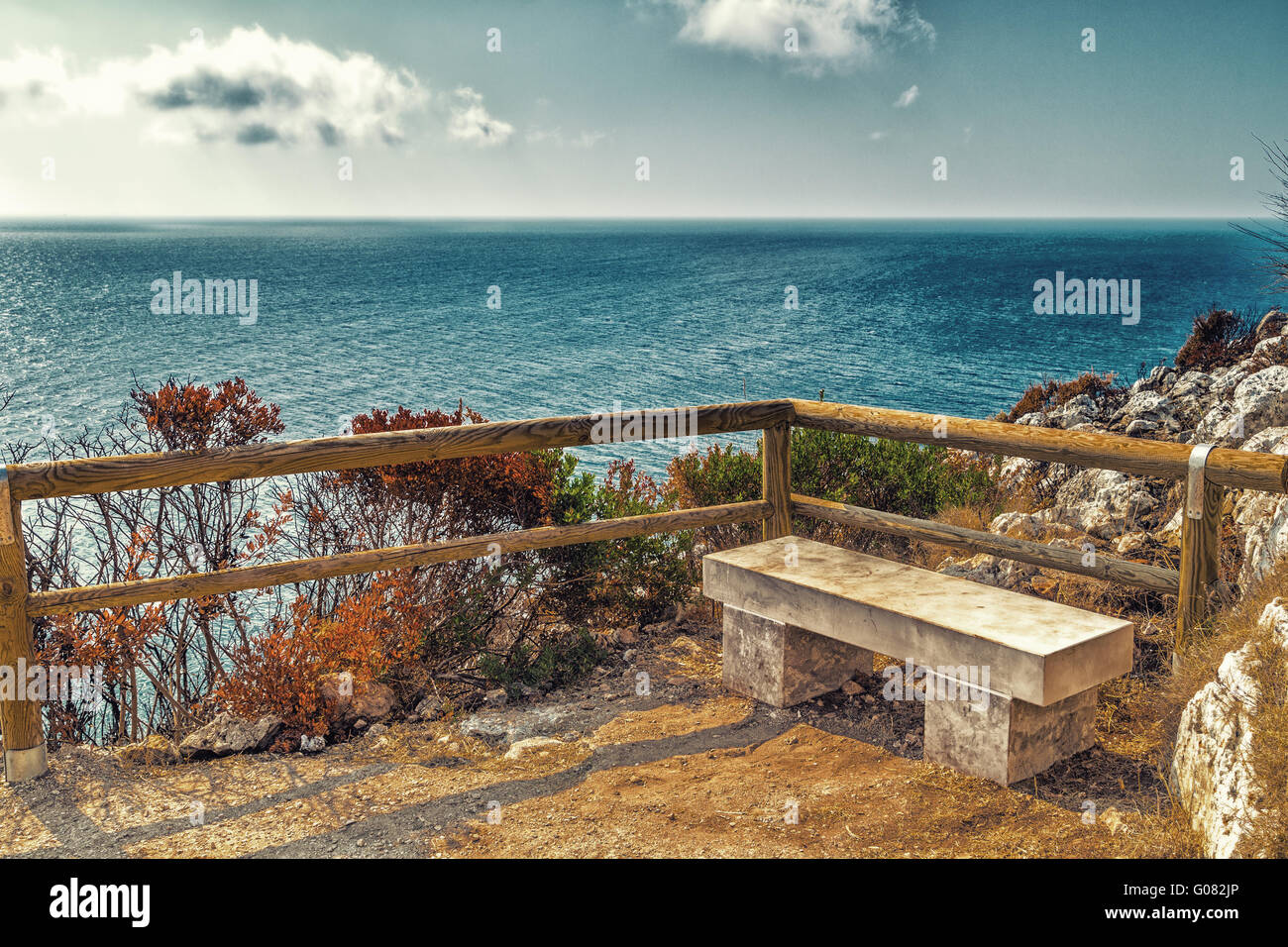 stone bench and wooden parapet on steep cliffs above the sea along the coast of Puglia in Italy ...