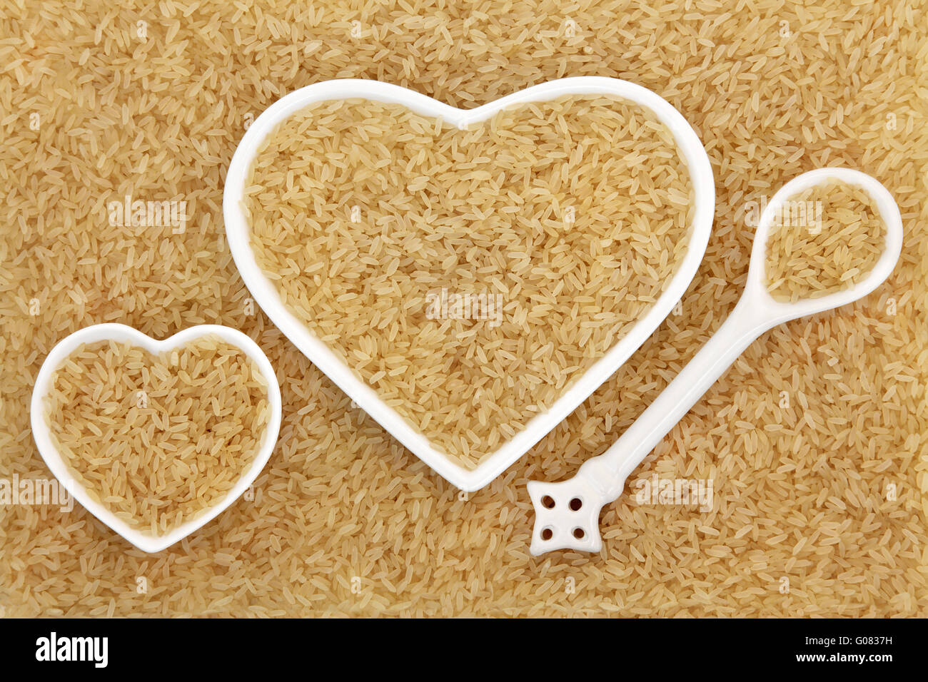 Long grain brown rice in heart shaped porcelain dishes and spoon ...