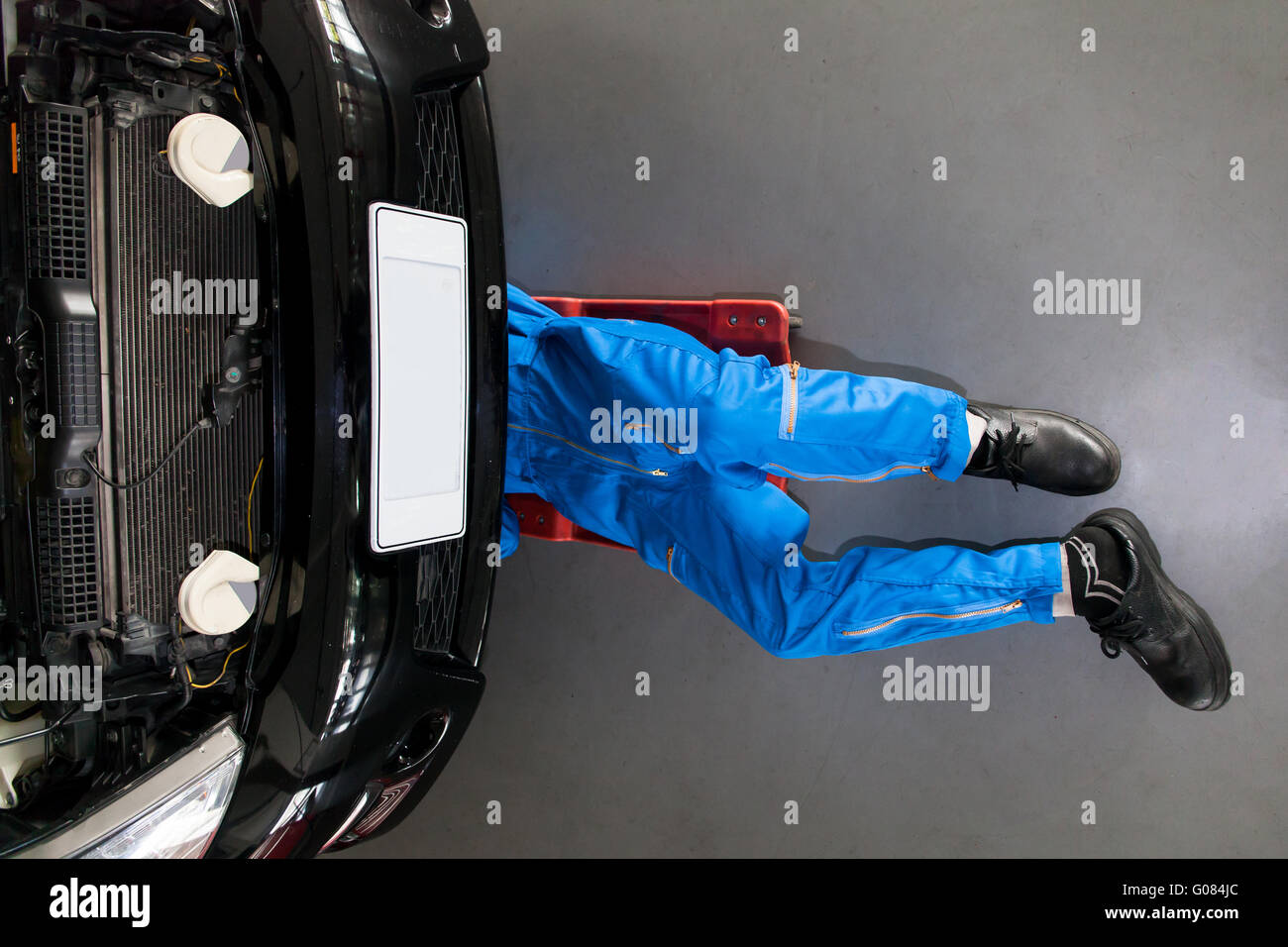 Mechanic in blue uniform lying down and working under car at the garage ...