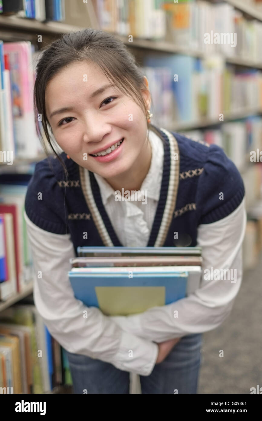 Young student holding books near bookshelf Stock Photo - Alamy