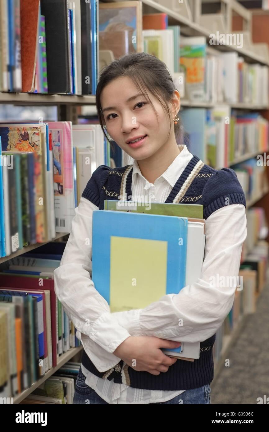 Young student holding books near bookshelf Stock Photo - Alamy