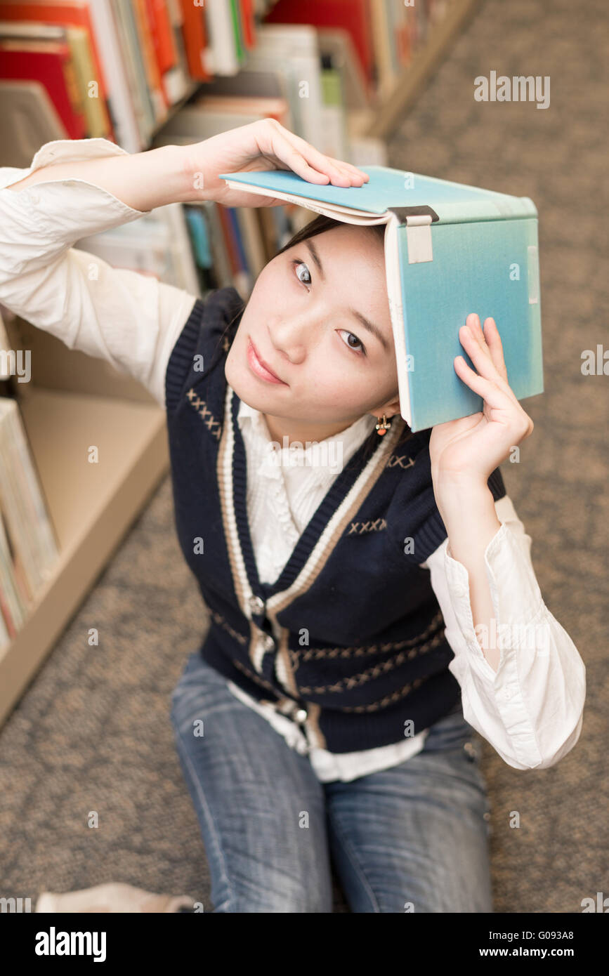 Girl holding a book over head near bookshelf Stock Photo - Alamy
