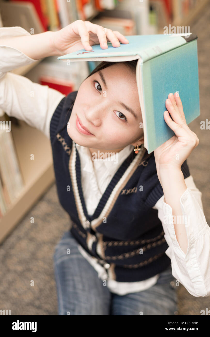 Girl holding a book over head near bookshelf Stock Photo - Alamy