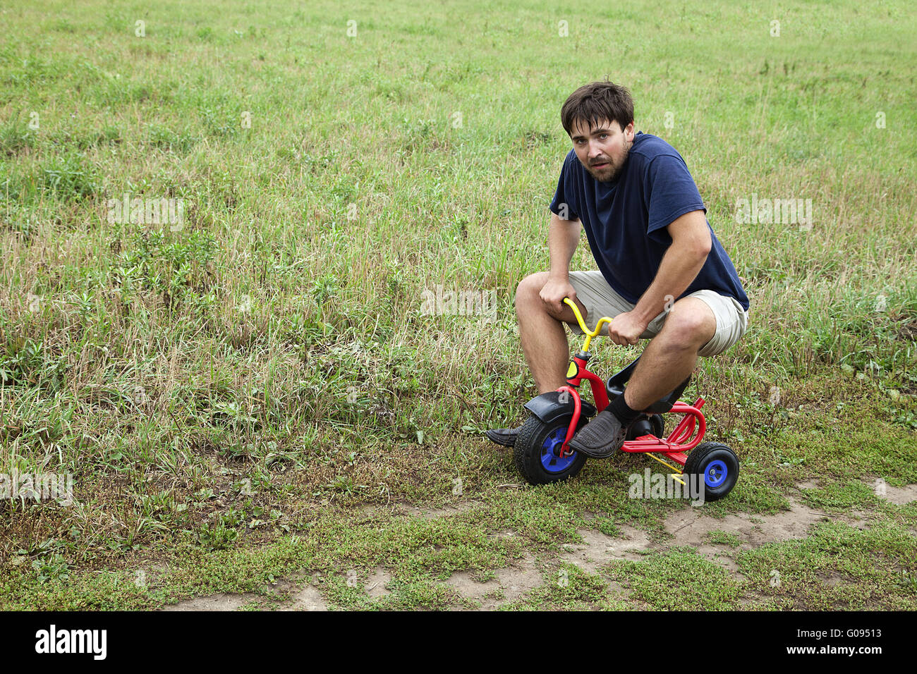 Adult man tying to ride on a small tricycle Stock Photo - Alamy