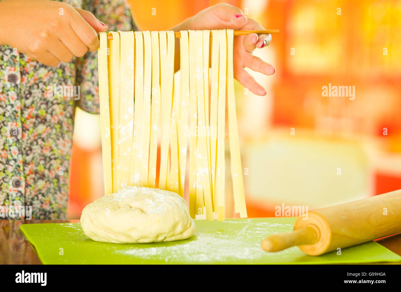 Fresh made spaghetti hanging across wooden stick being held by woman ...