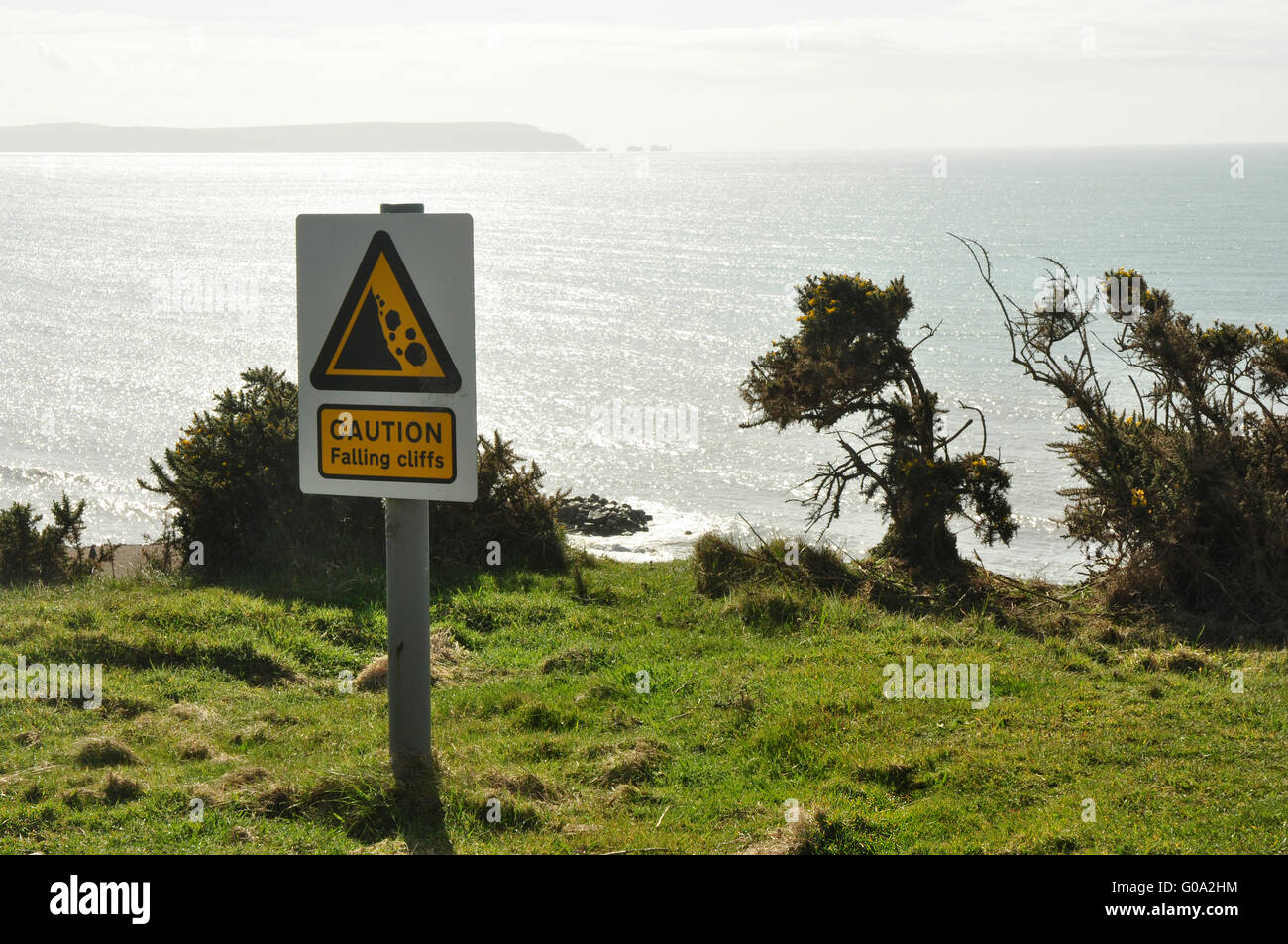Caution -falling cliffs - warning sign on pathway above a sunlit sea ...