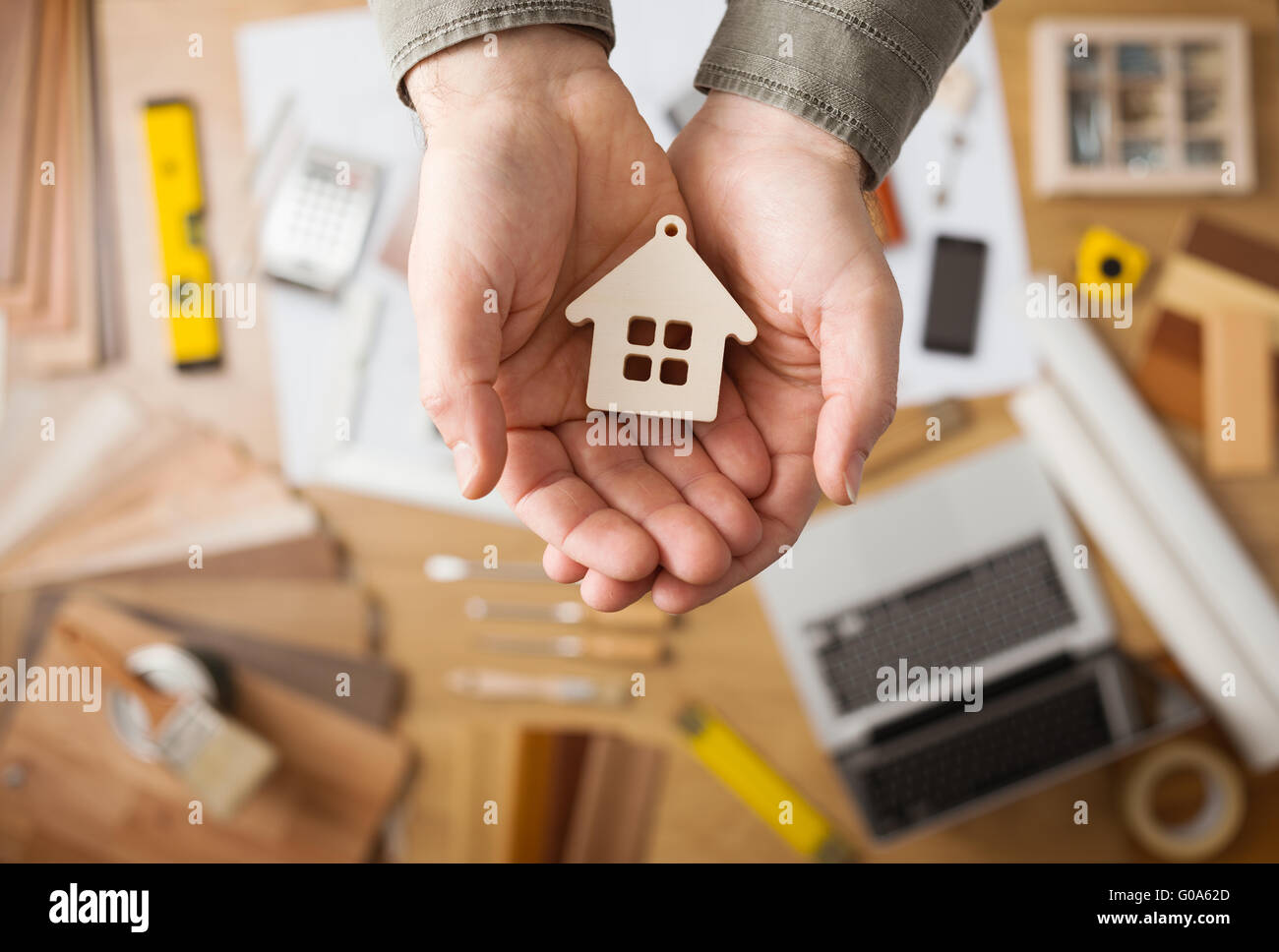 Real estate agent holding a small house, desktop with tools, wood ...