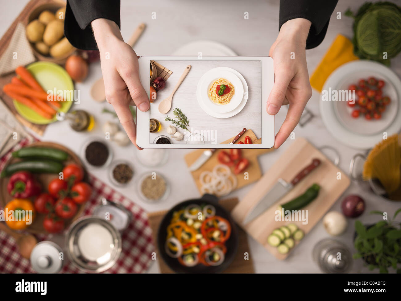 Cook's hands holding a touch screen tablet close up, kitchen table with ...