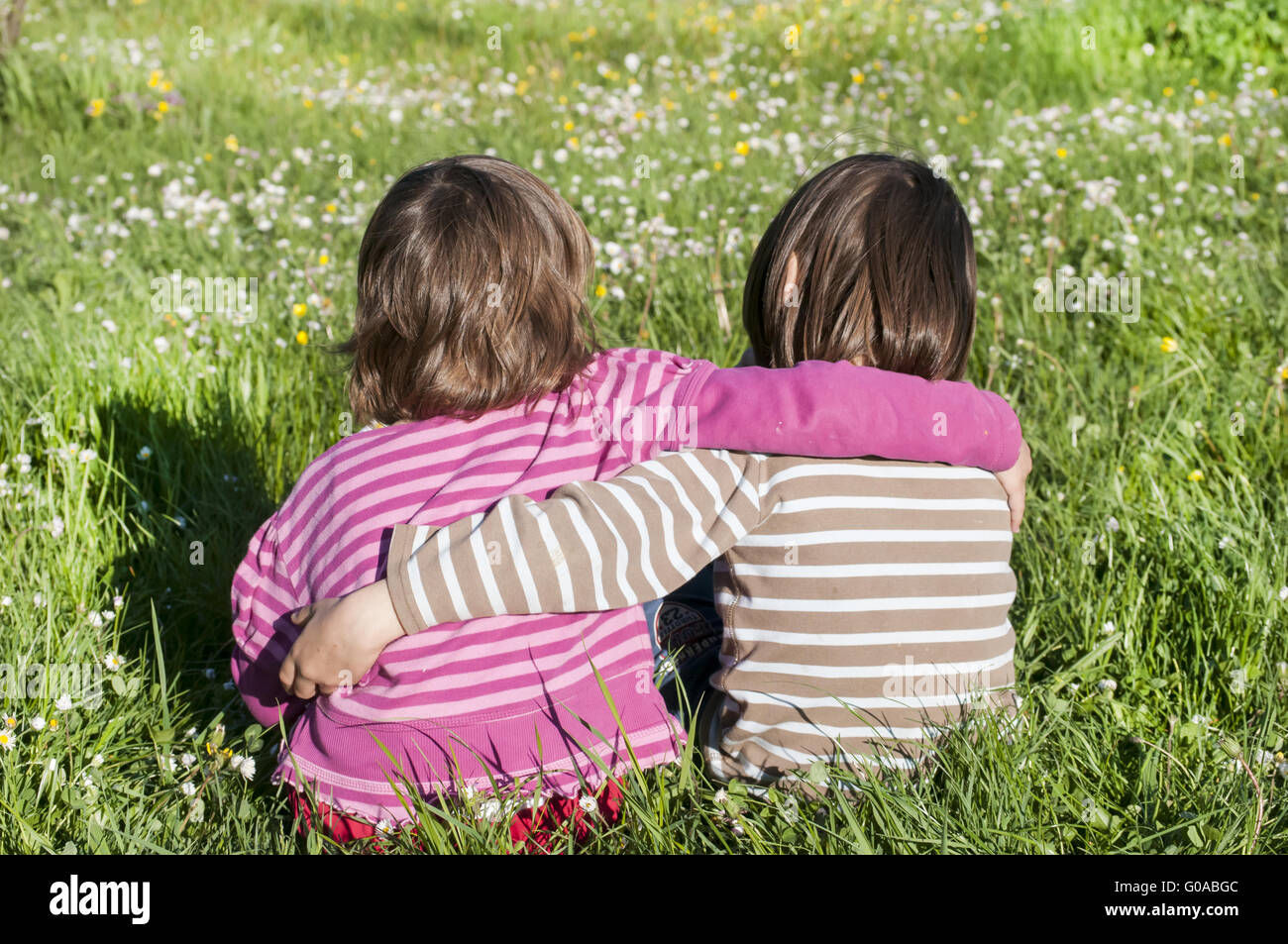 Two children sitting back together on rural meadow Stock Photo - Alamy