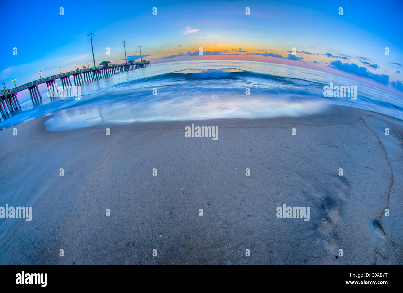 The rising sun peeks through clouds and is reflected in waves by the ...