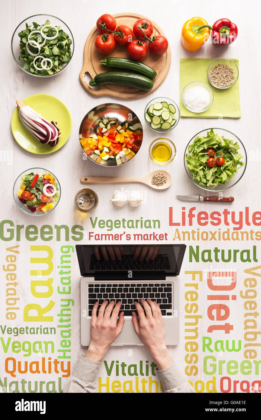 Hands typing on a laptop with fresh vegetables and healthy eating text ...
