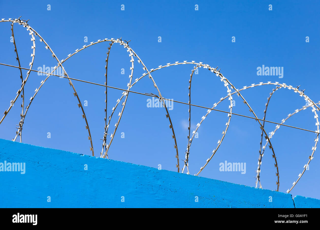 Barbed wire on the fence against a blue sky background Stock Photo - Alamy