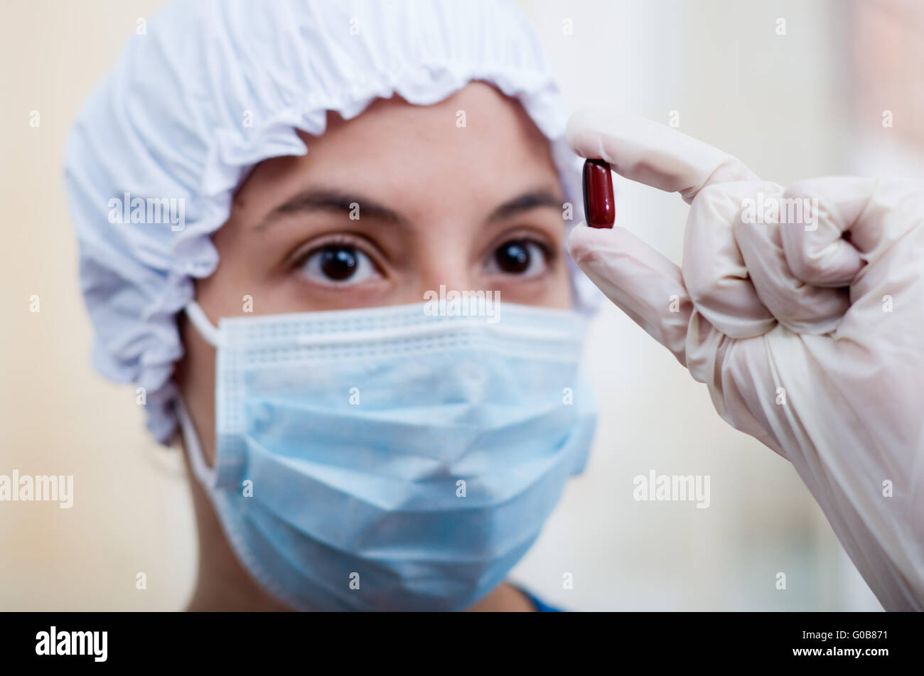 Nurse wearing bouffant cap and facial mask holding up brown pill ...