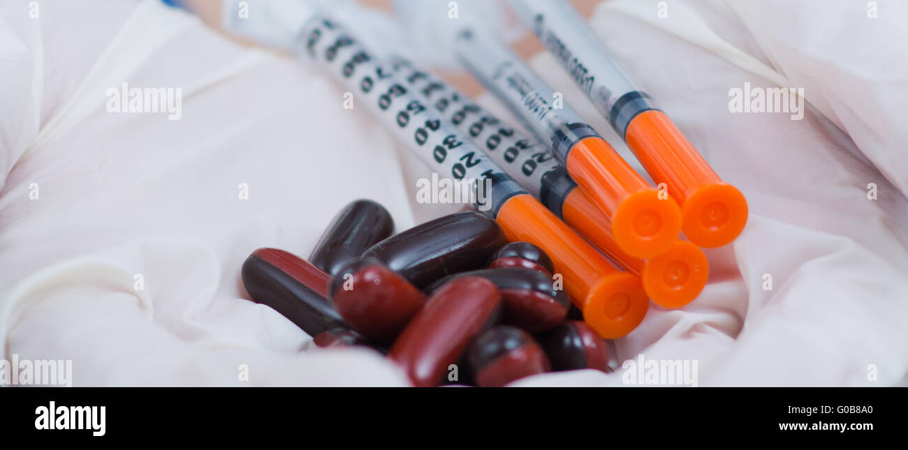 Closeup syringes and pill capsules lying in small pile on white fabric ...