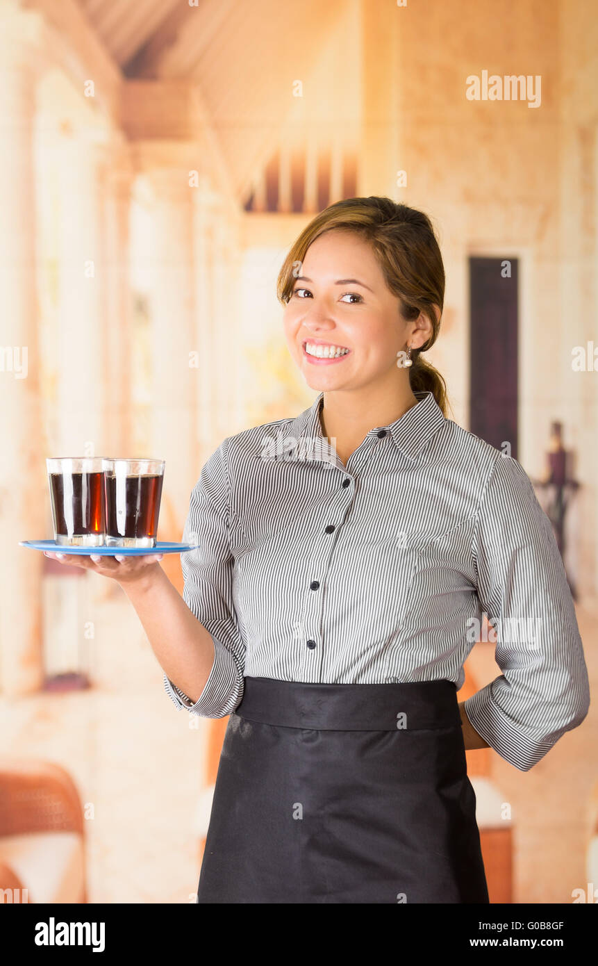 Young brunette waitress wearing uniform with friendly smile, holding up ...
