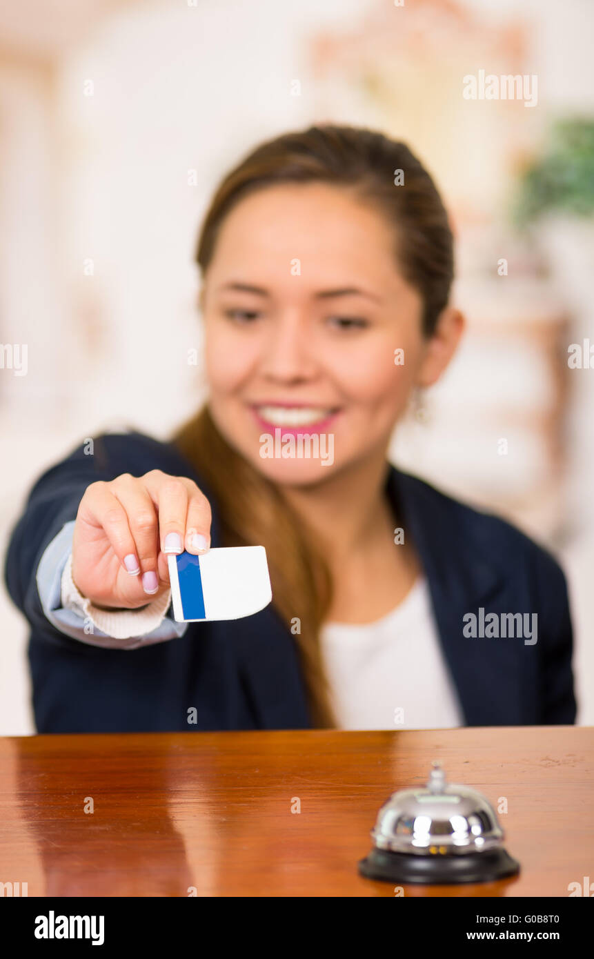 Young brunette hotel receptionist with friendly smile handing over key ...
