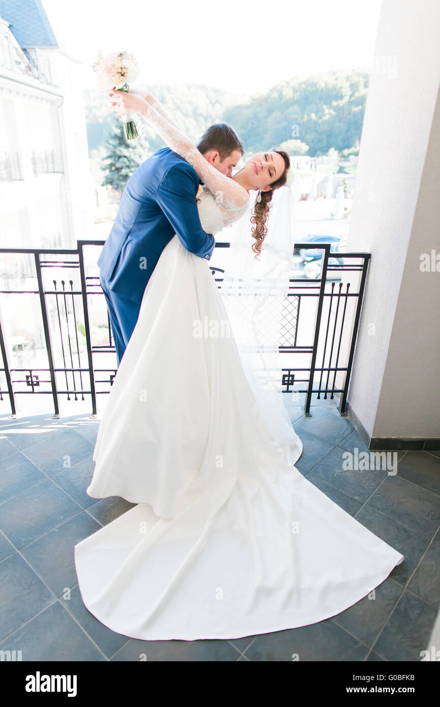 Handsome groom kissing neck of beautiful young bride on the balcony in ...