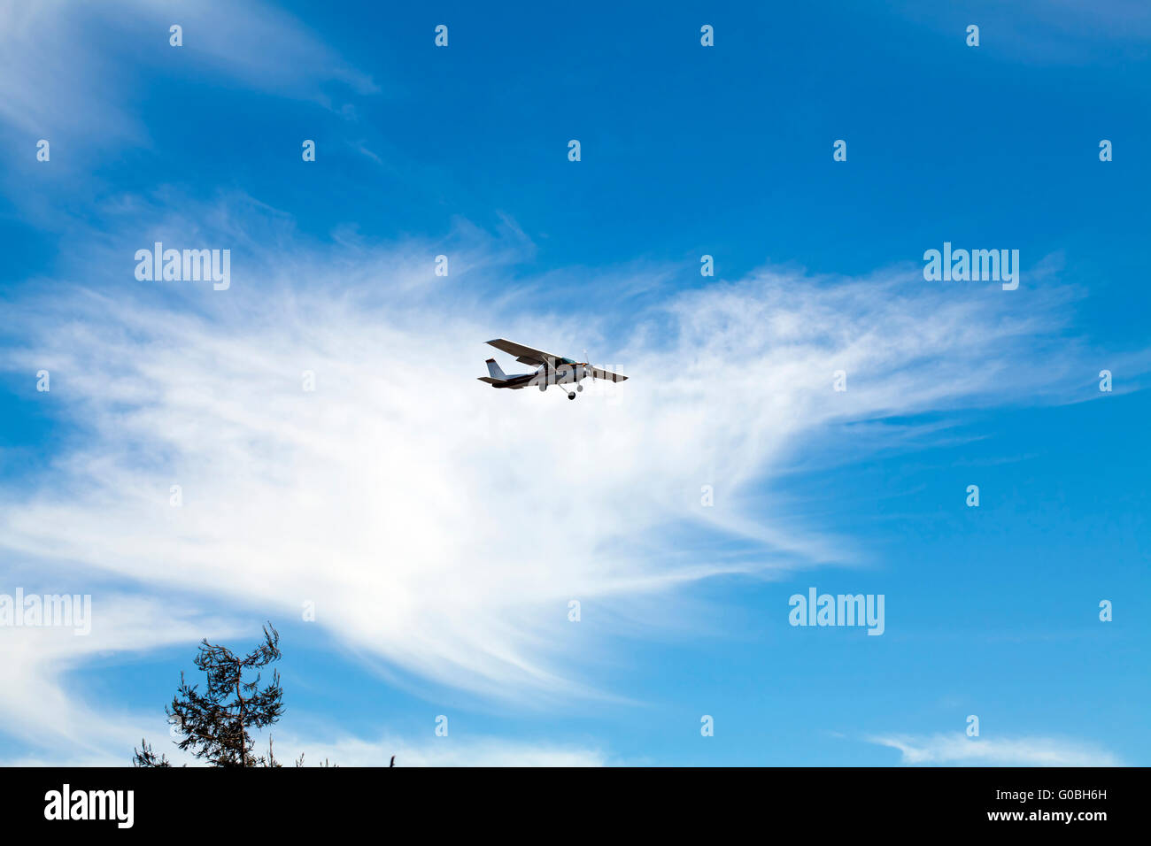 horizontal shot of small plane in blue sky and white cirrus clouds ...