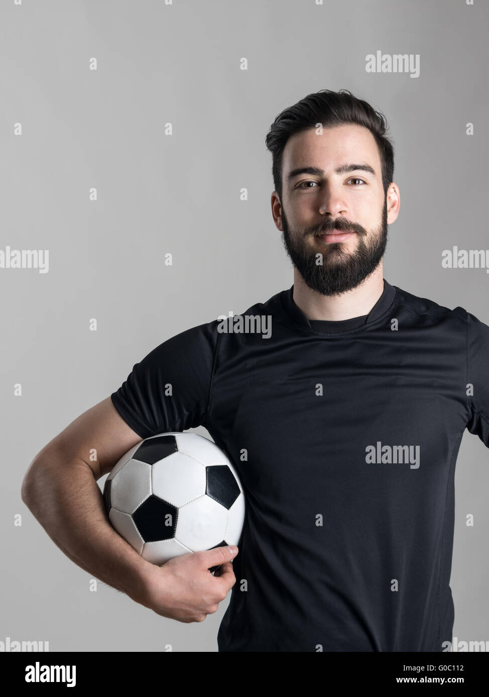 Friendly smiling bearded soccer player holding ball under his arm ...