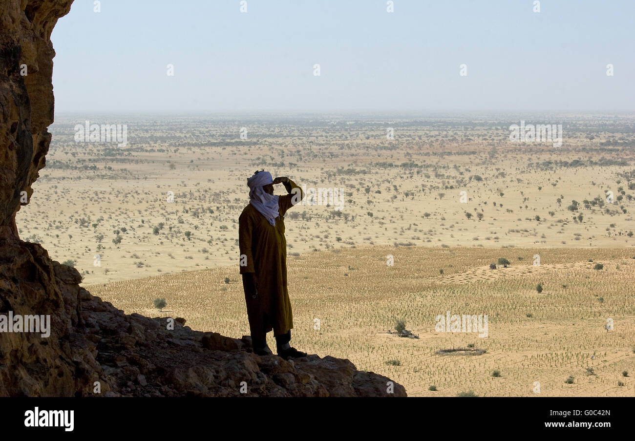 Man on rock overlooking countryside in Sacred mountain. Sahel. Niger ...