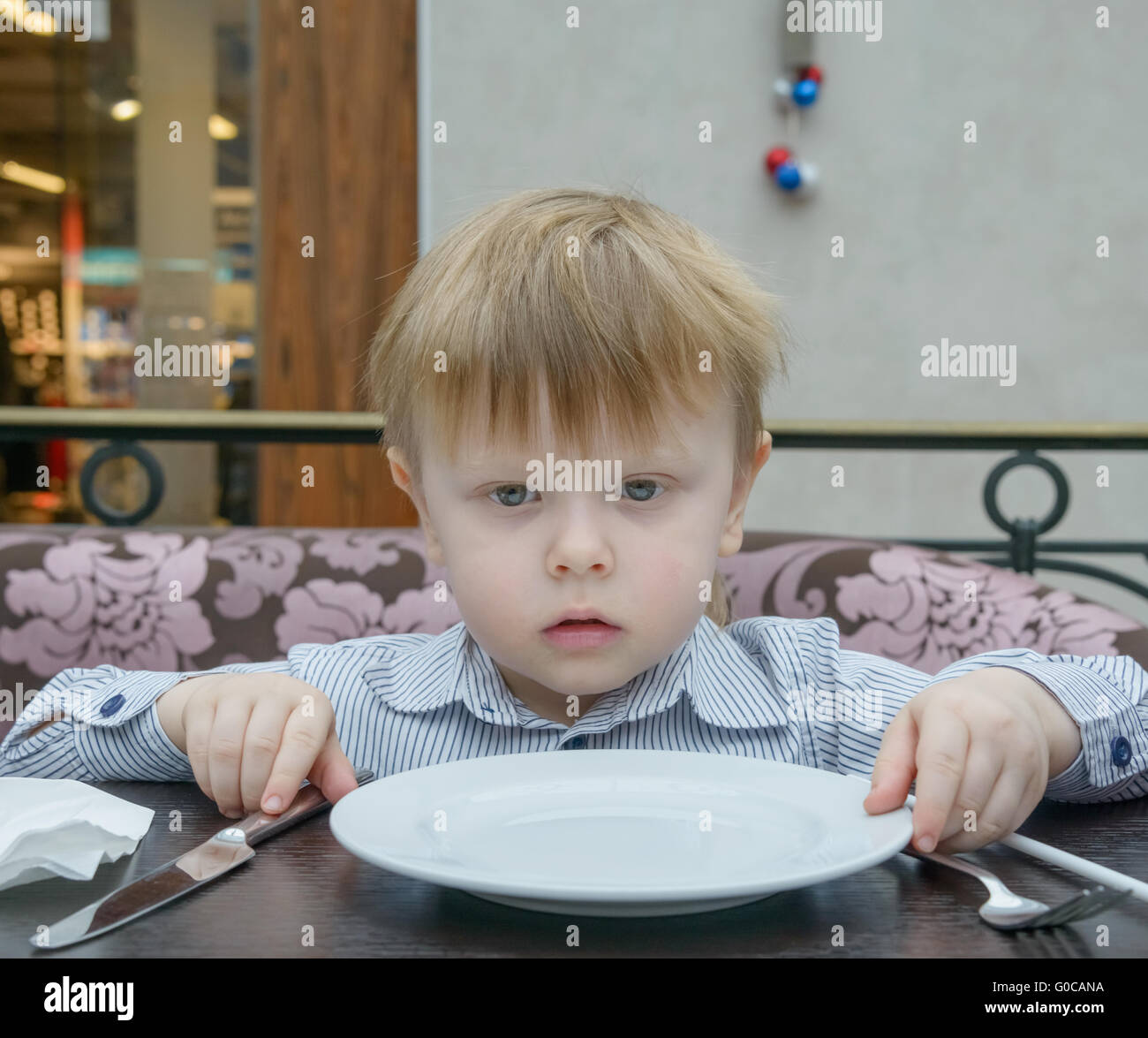 blond boy sitting at a table with an empty plate Stock Photo - Alamy
