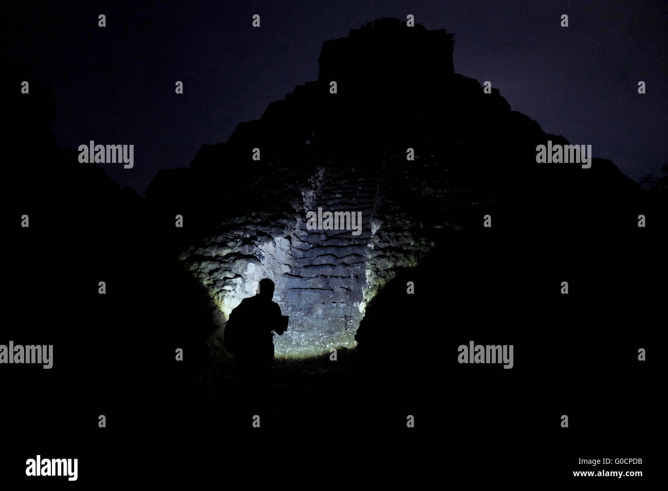 A hiker illuminating with a torch the ancient Mayan stepped pyramid ...
