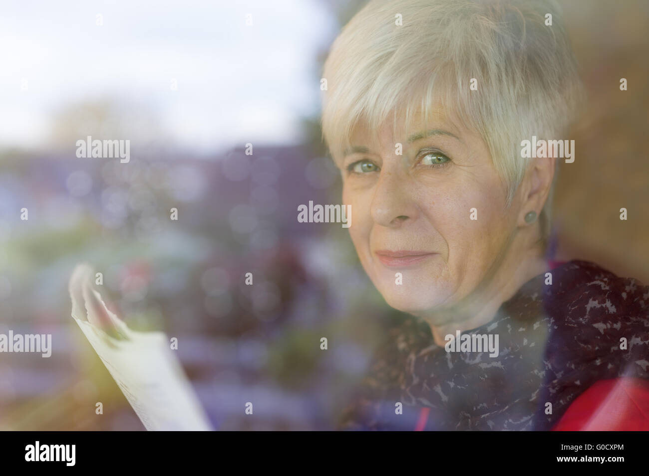 Elderly lady sitting behind a glass window and hol Stock Photo - Alamy