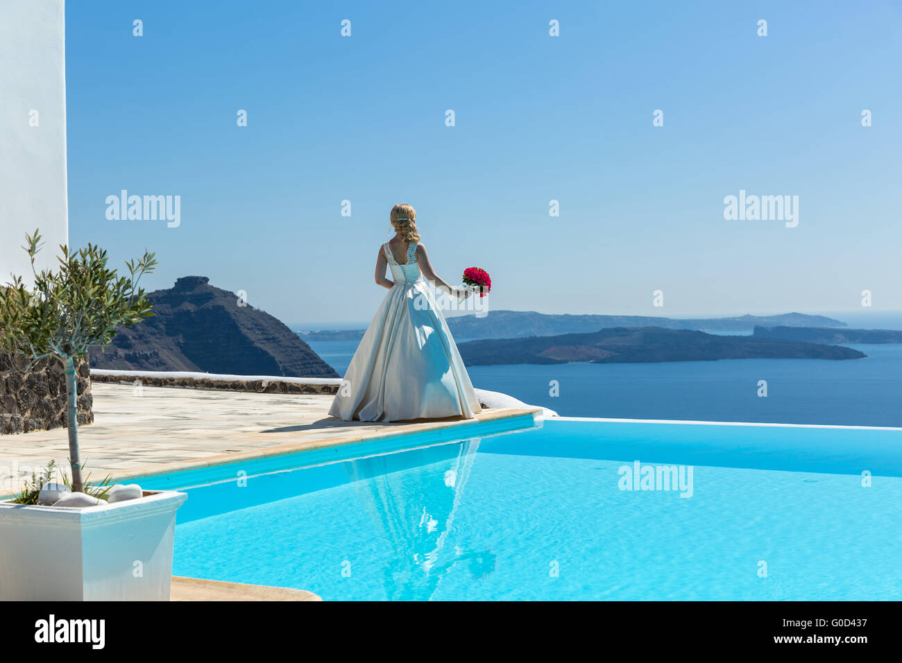 Bride in a beautiful dress standing near the pool looking at the sea ...