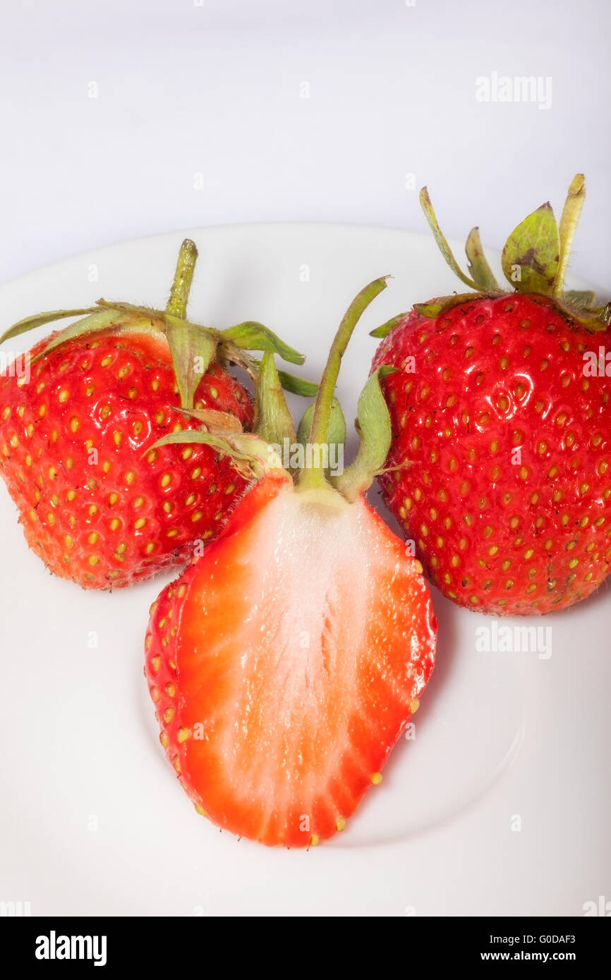Half of ripe and juicy strawberries on a plate with two whole berries ...