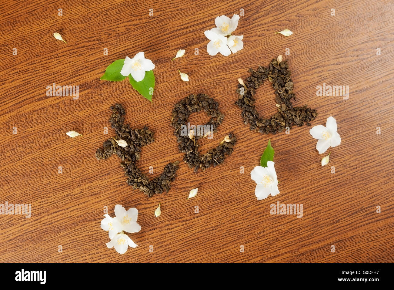 the word tea from leaves of green tea on a wooden surface near jasmine ...