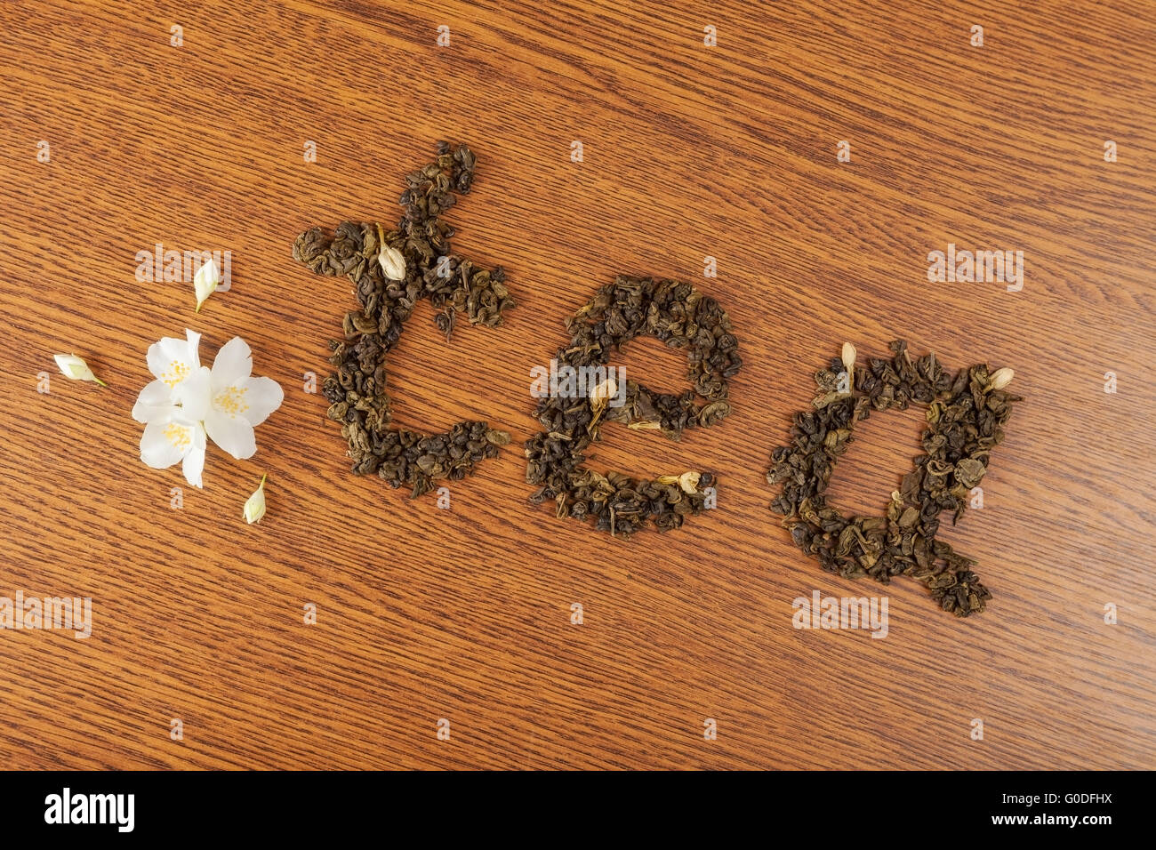 the word tea from leaves of green tea on a wooden surface near jasmine ...