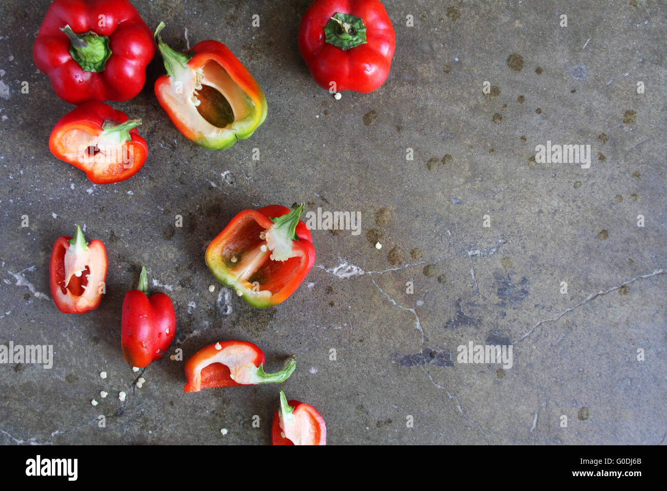 Overhead view of whole and sliced red peppers on a grey stone slab with ...