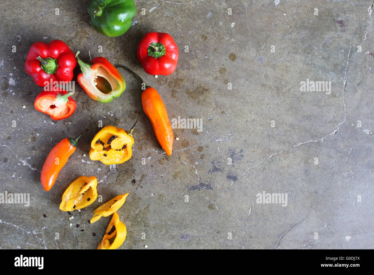 Overhead view of colorful whole and sliced hot peppers on a stone slab ...
