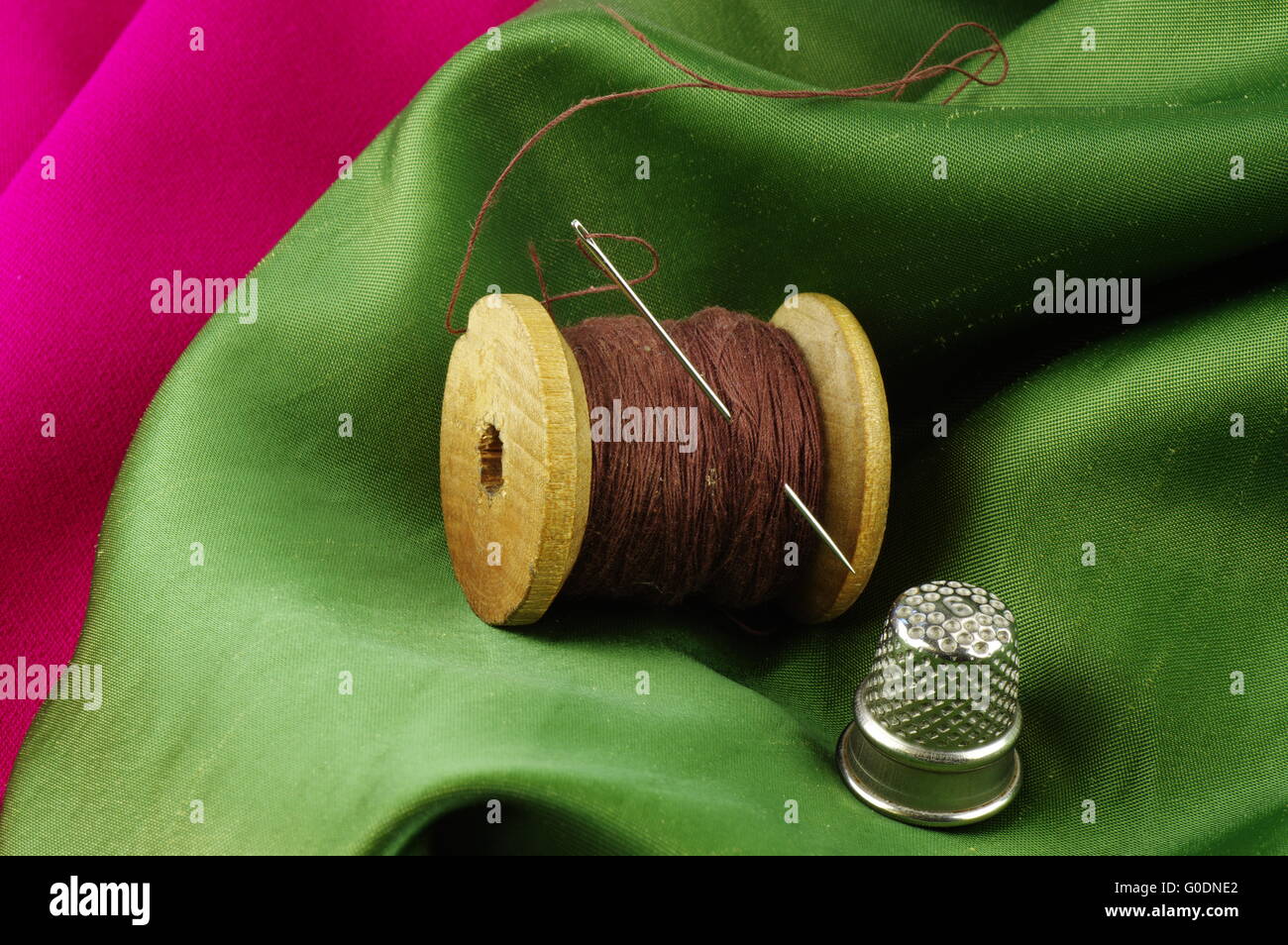 Wooden spool of thread with a needle and a thimble on a colored ...