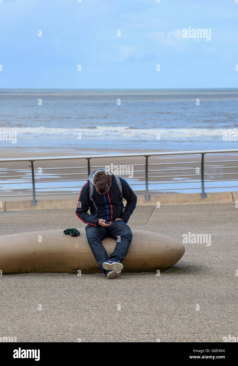 Young man bending his head and looking at his smartphone whilst sitting ...